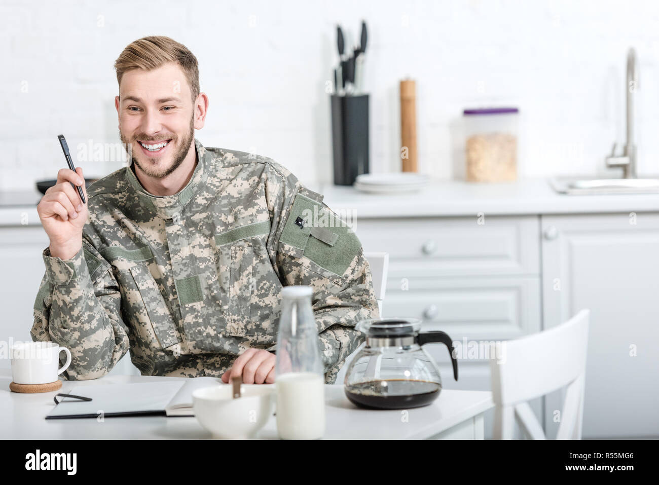 smiling army soldier sitting at kitchen table with pen and notebook ...
