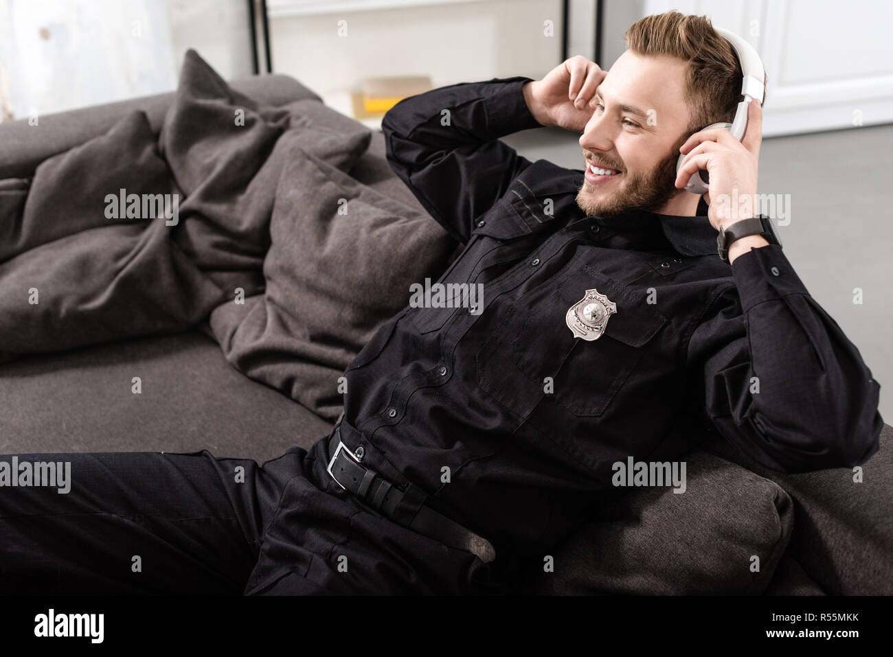 Smiling policeman sitting on couch and putting on headphones Stock ...