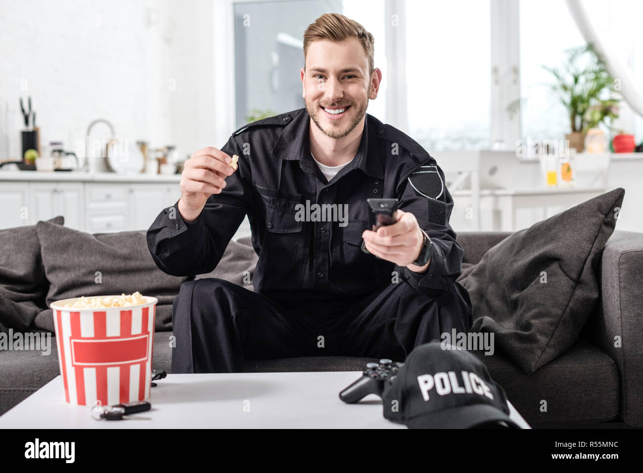 police officer sitting on couch, holding remote control and eating ...