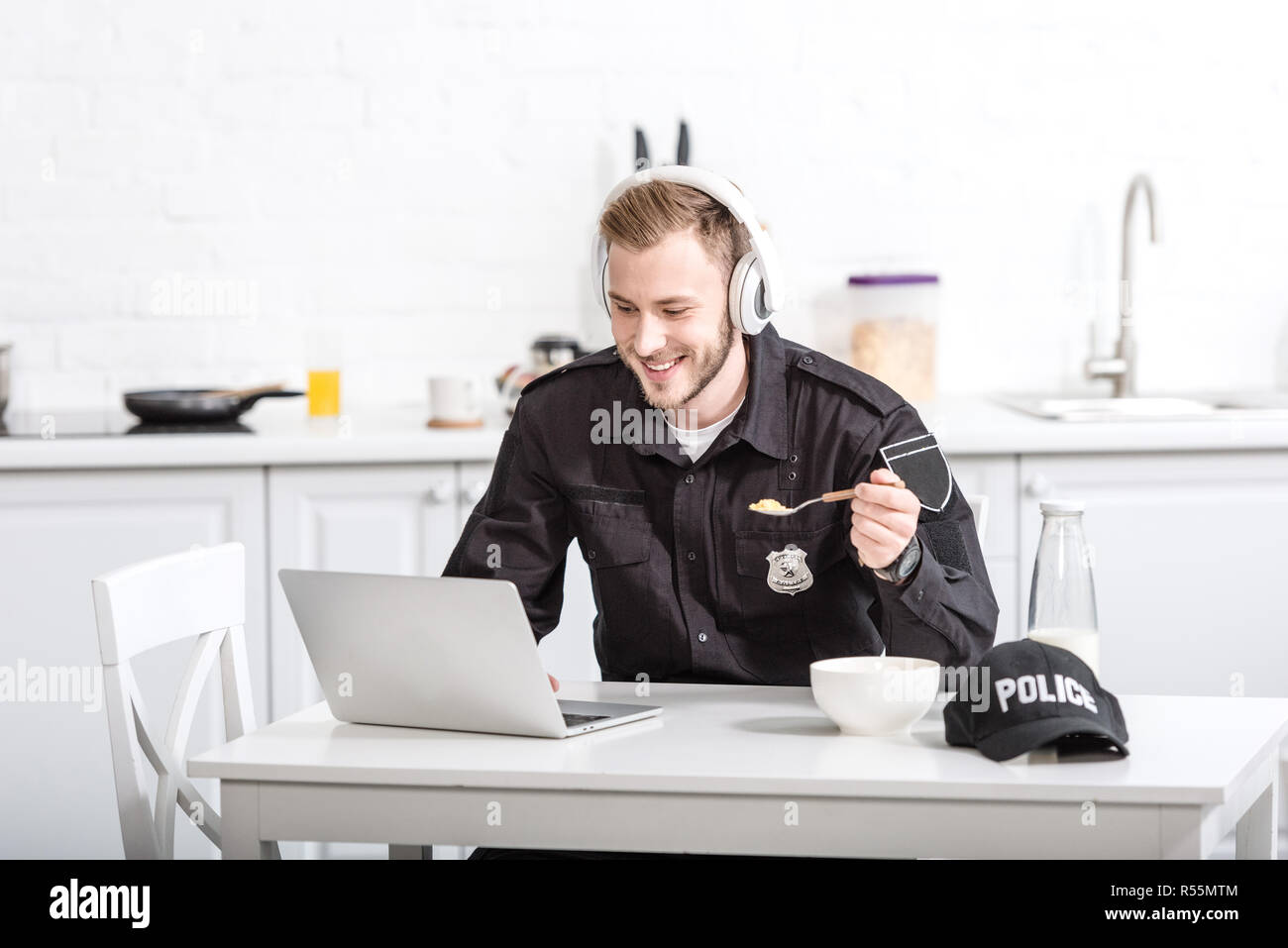 Handsome police officer eating cornflakes and using laptop at kitchen ...
