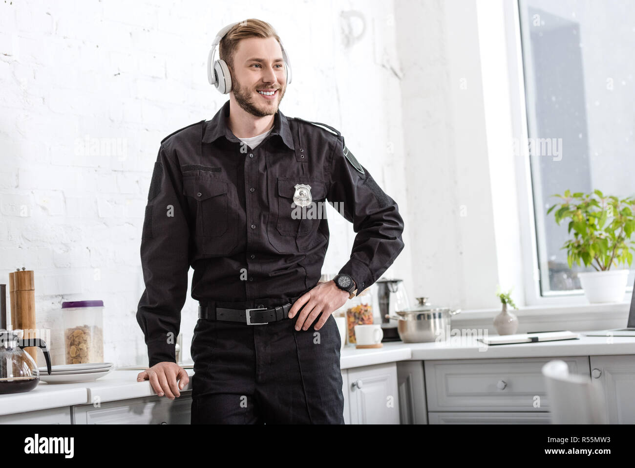 smiling police officer listening to music with headphones at kitchen ...