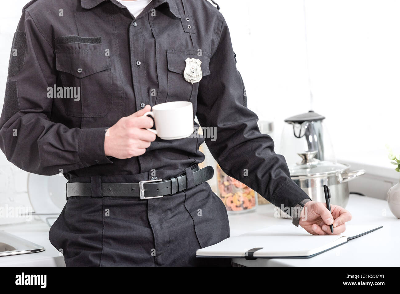 police officer drinking coffee and writing in notebook at kitchen table ...