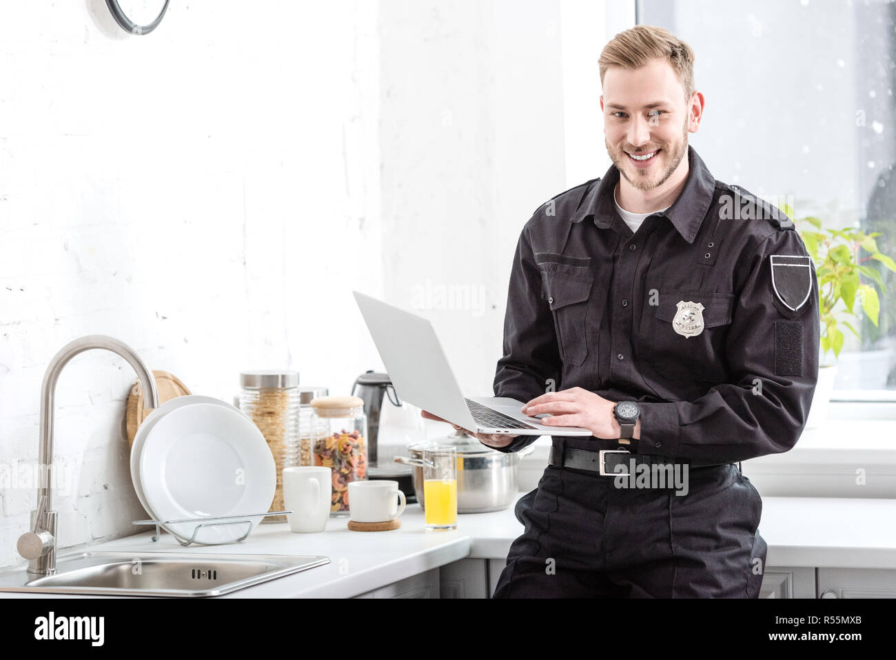 Smiling police officer standing with laptop at kitchen Stock Photo - Alamy