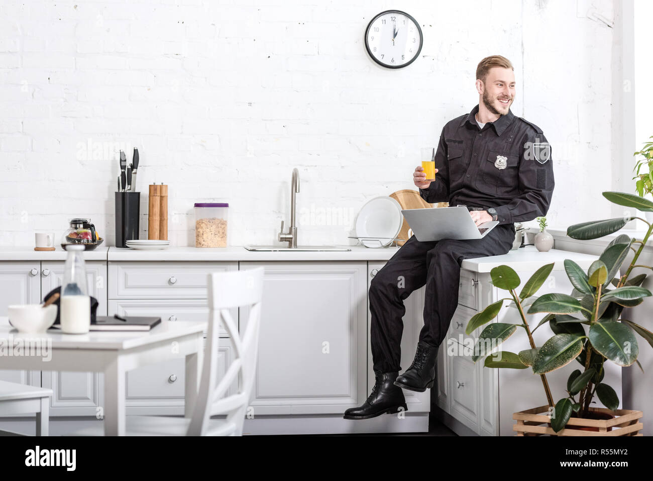 smiling man in police uniform sitting on kitchen table, drinking orange ...