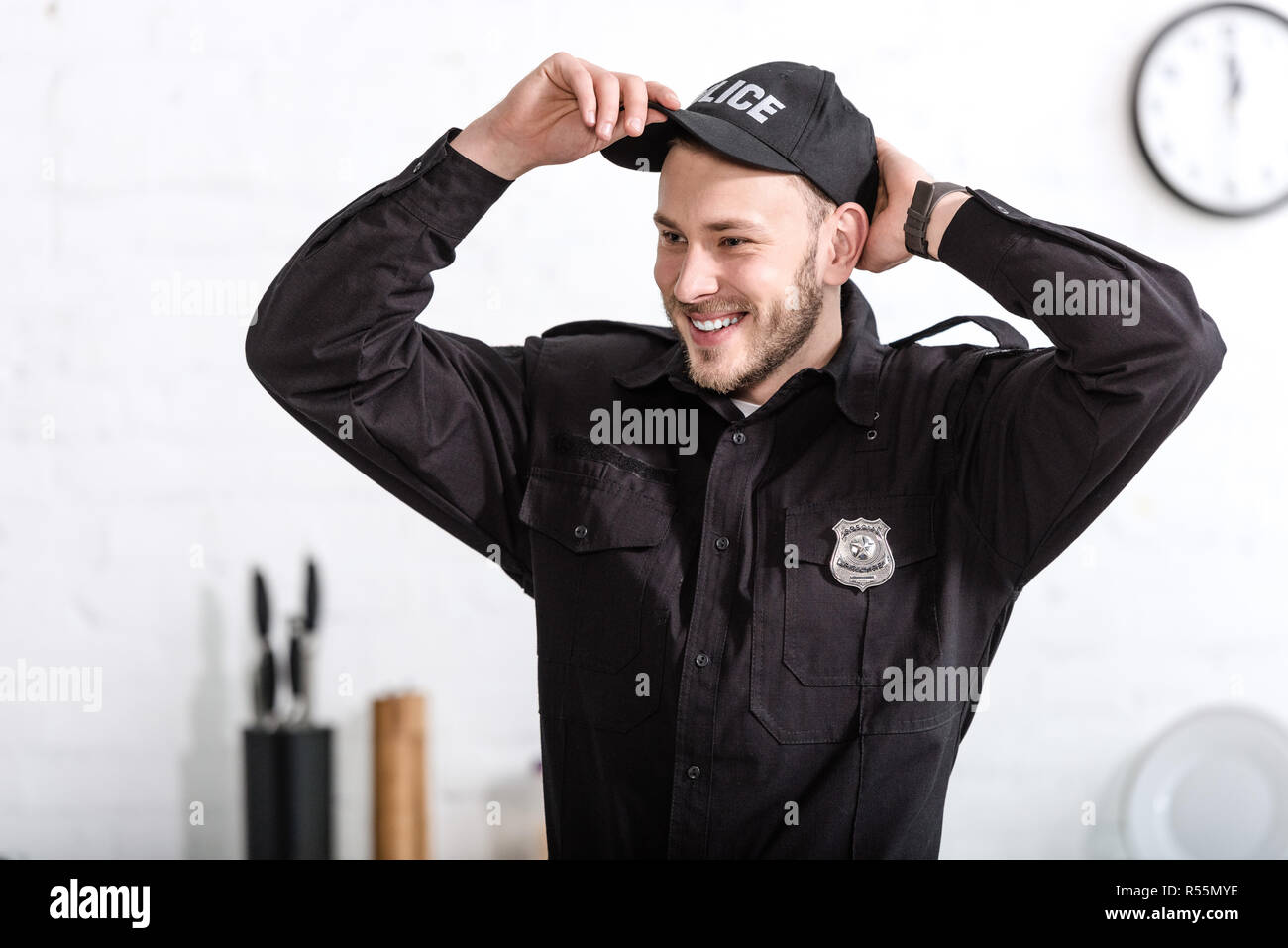handsome police officer smiling and putting on cap at kitchen Stock ...