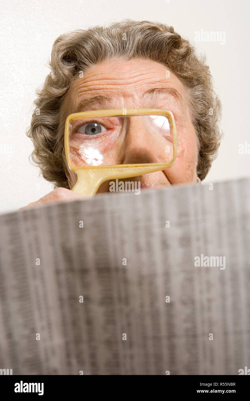Woman reading newspaper with magnifying glass Stock Photo - Alamy