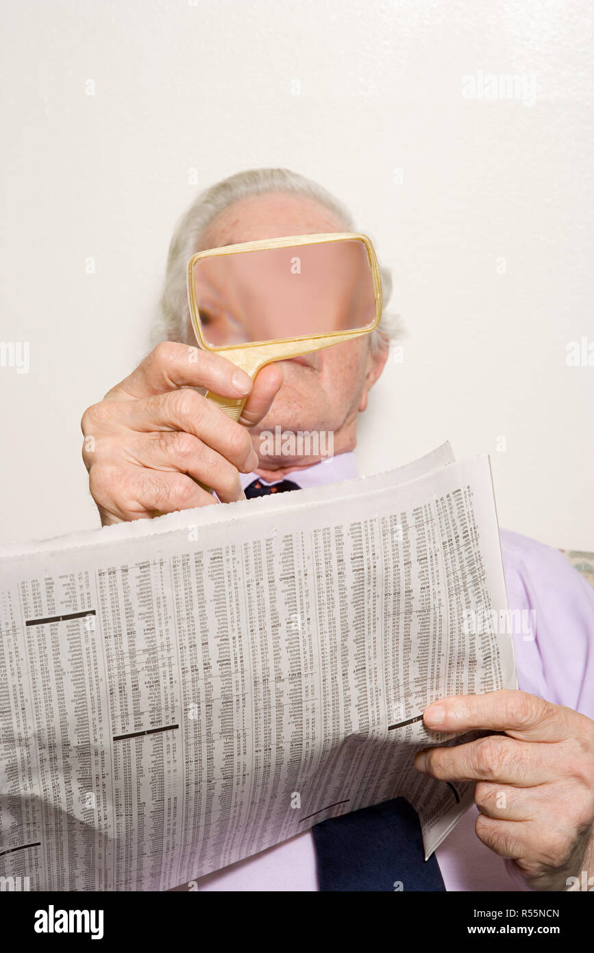 Man reading newspaper with magnifying glass Stock Photo - Alamy