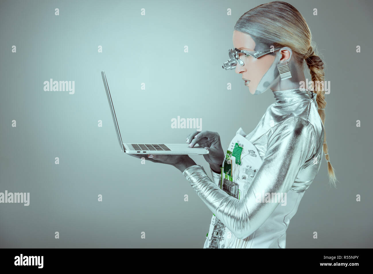 side view of silver robot holding laptop isolated on grey, future ...