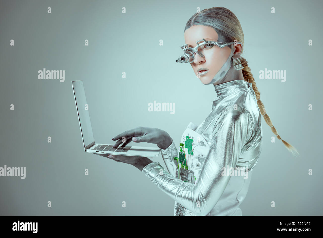 side view of silver robot holding laptop and looking at camera isolated ...