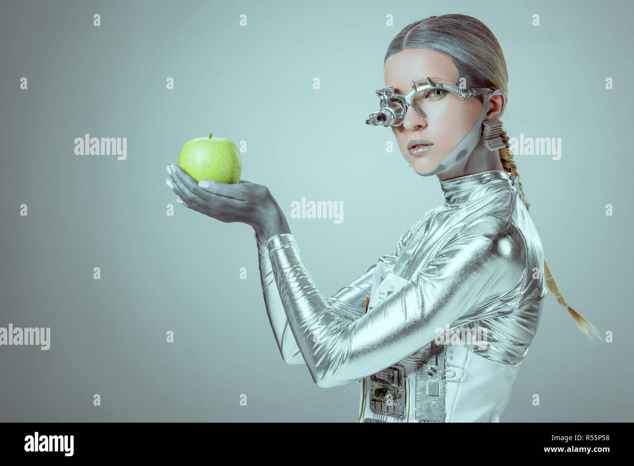 side view of cyborg holding green apple and looking at camera isolated ...