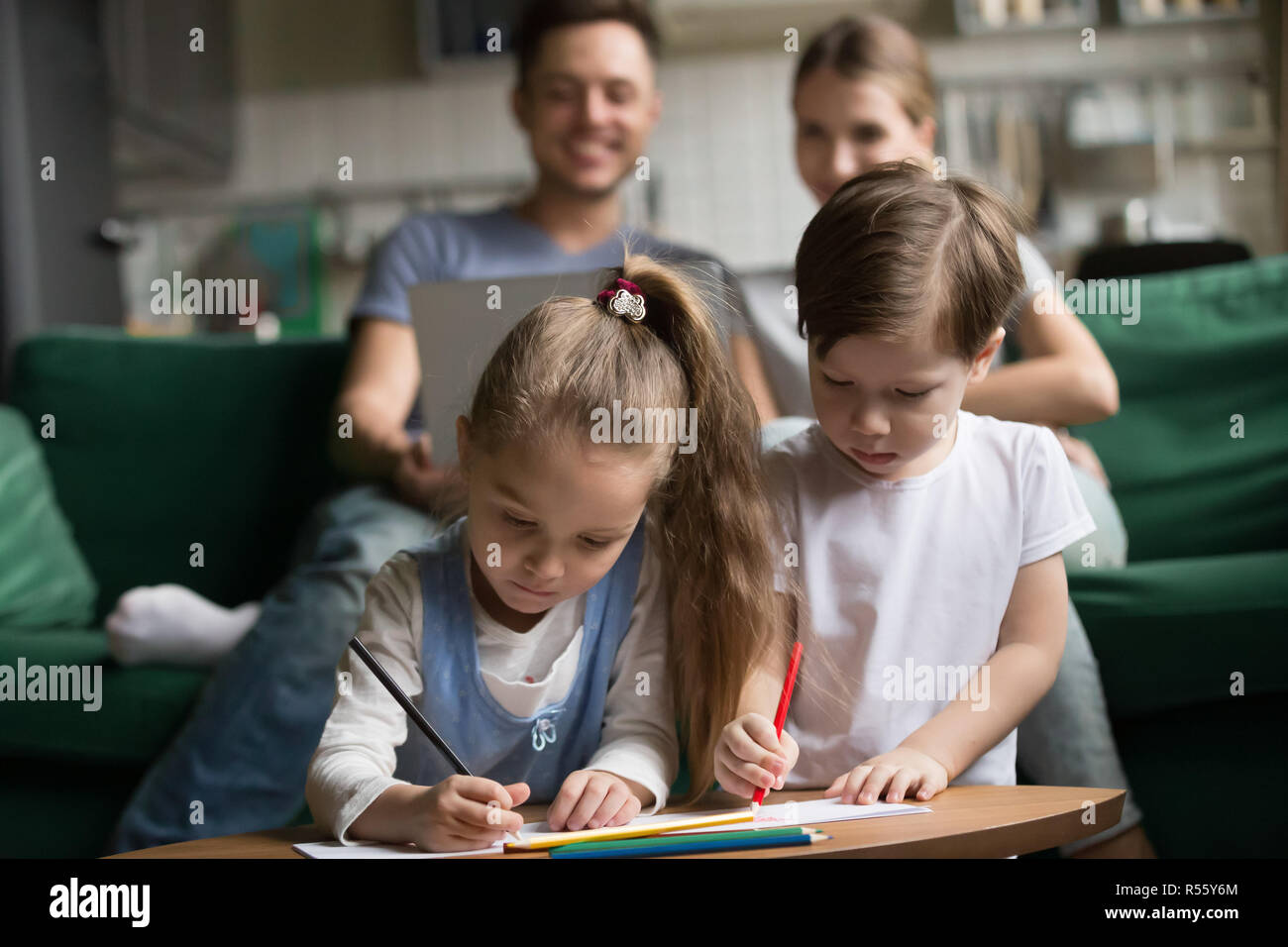 Children drawing with colored pencils while parents using laptop Stock ...