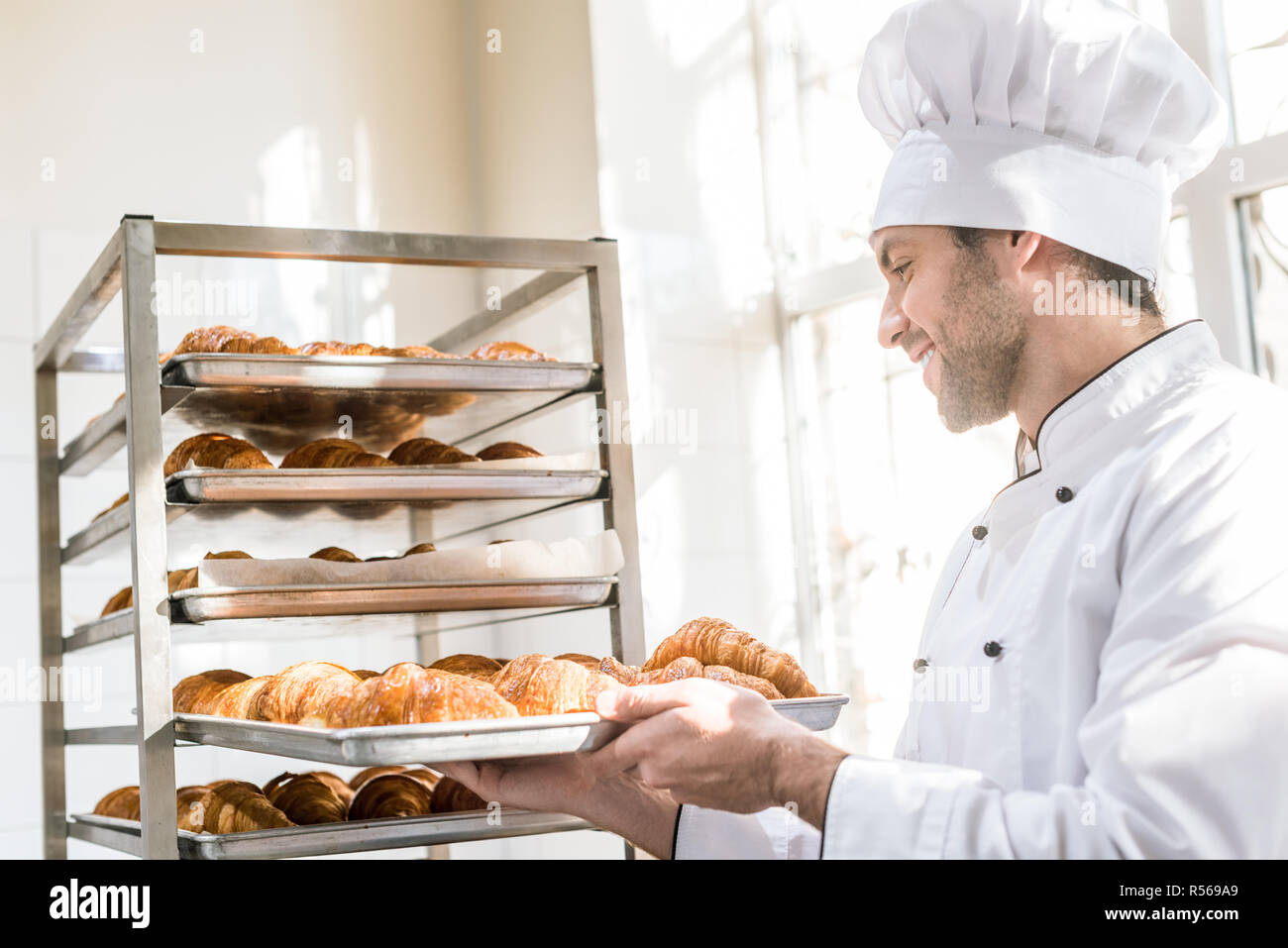 Side view of smiling baker taking tray with pastry Stock Photo - Alamy