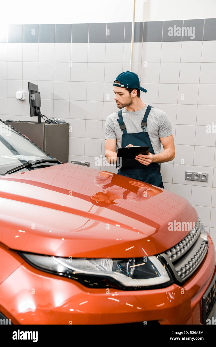 portrait of focused auto mechanic with notepad examining car at auto ...