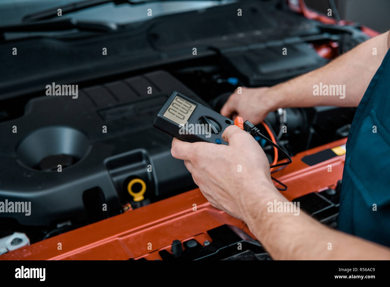 partial view of auto mechanic with multimeter voltmeter checking car ...