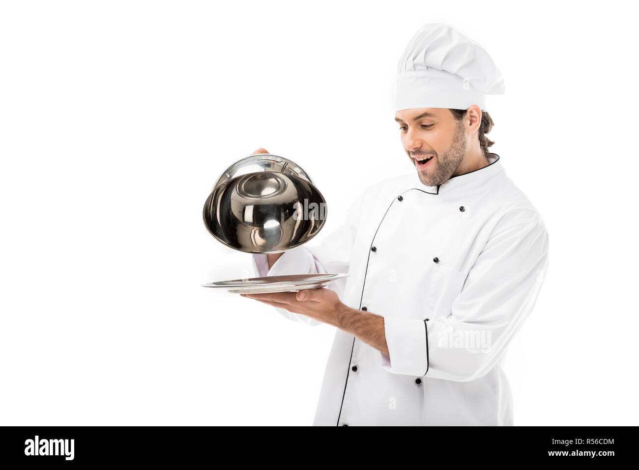 surprised young chef taking of serving dome from plate isolated on ...