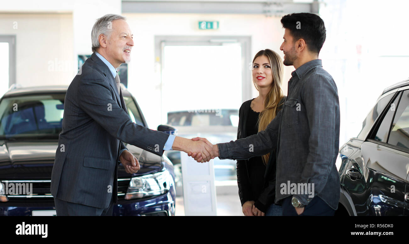 Car dealer giving a handshake to a young couple Stock Photo - Alamy