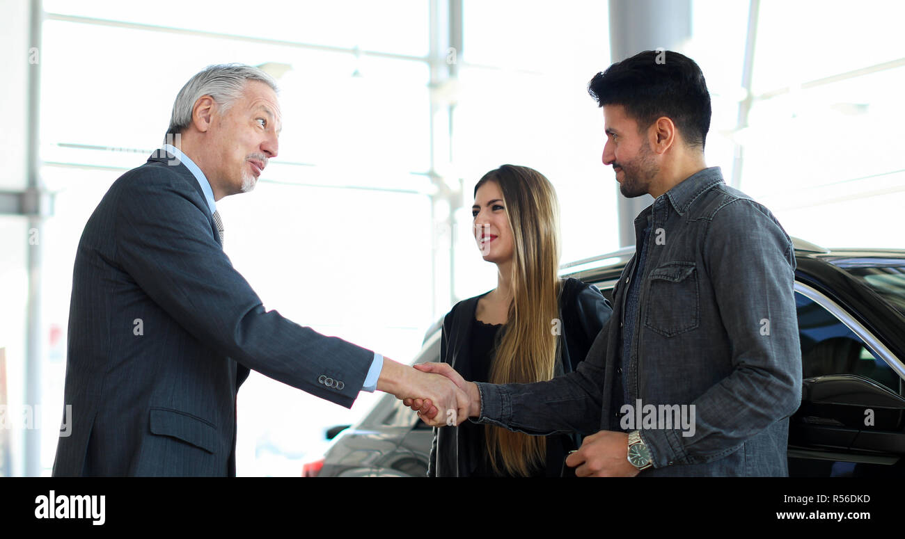 Car dealer giving a handshake to a young couple Stock Photo - Alamy