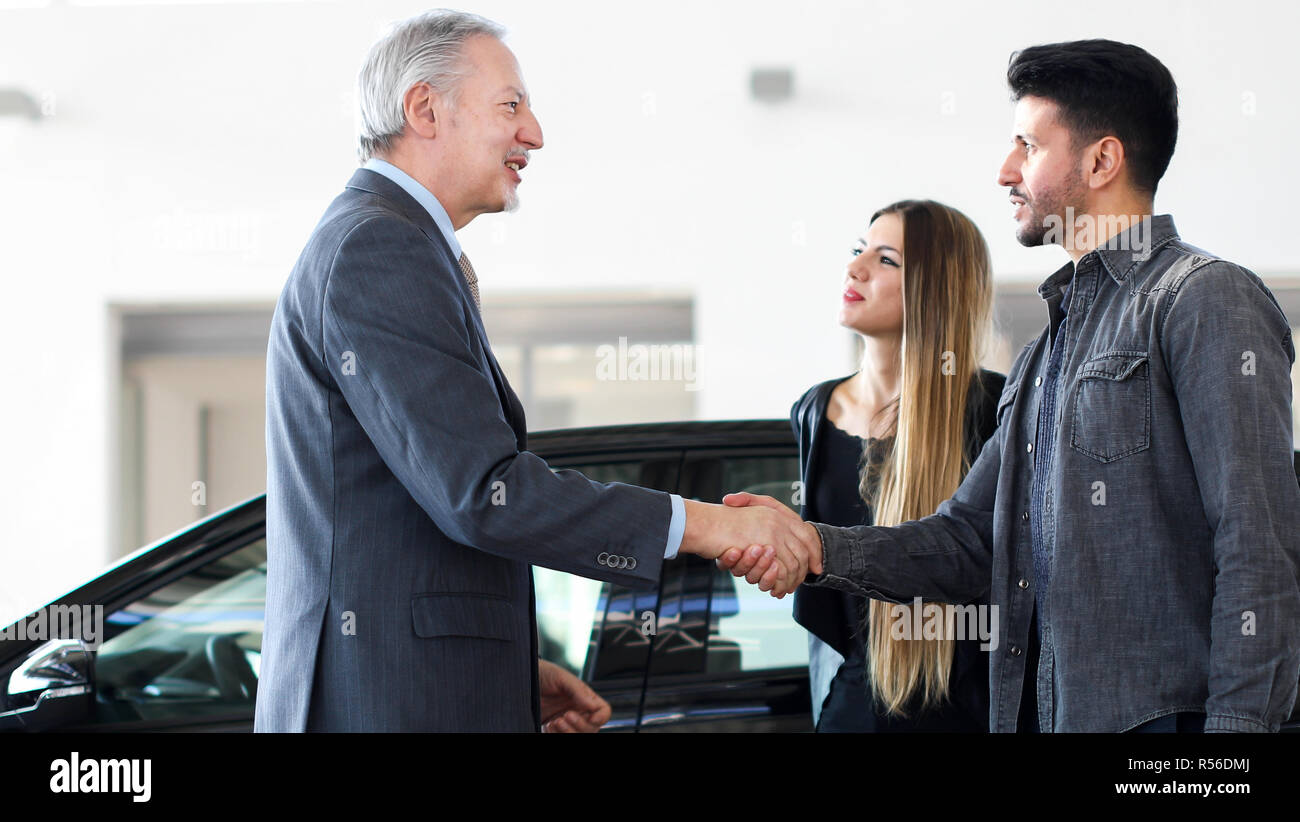 Car dealer giving a handshake to a young couple Stock Photo - Alamy