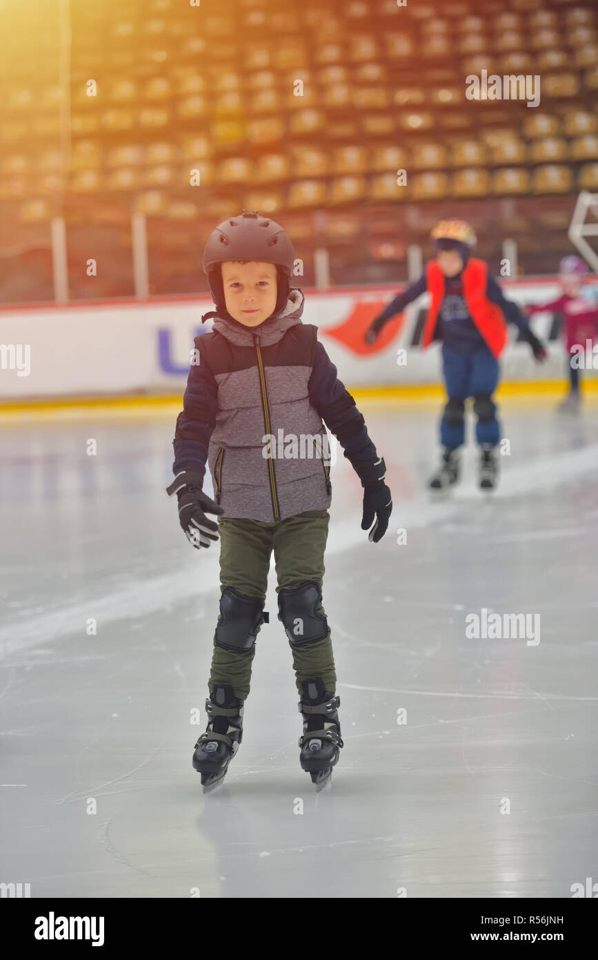 Adorable little boy in winter clothes with protections skating on ice ...