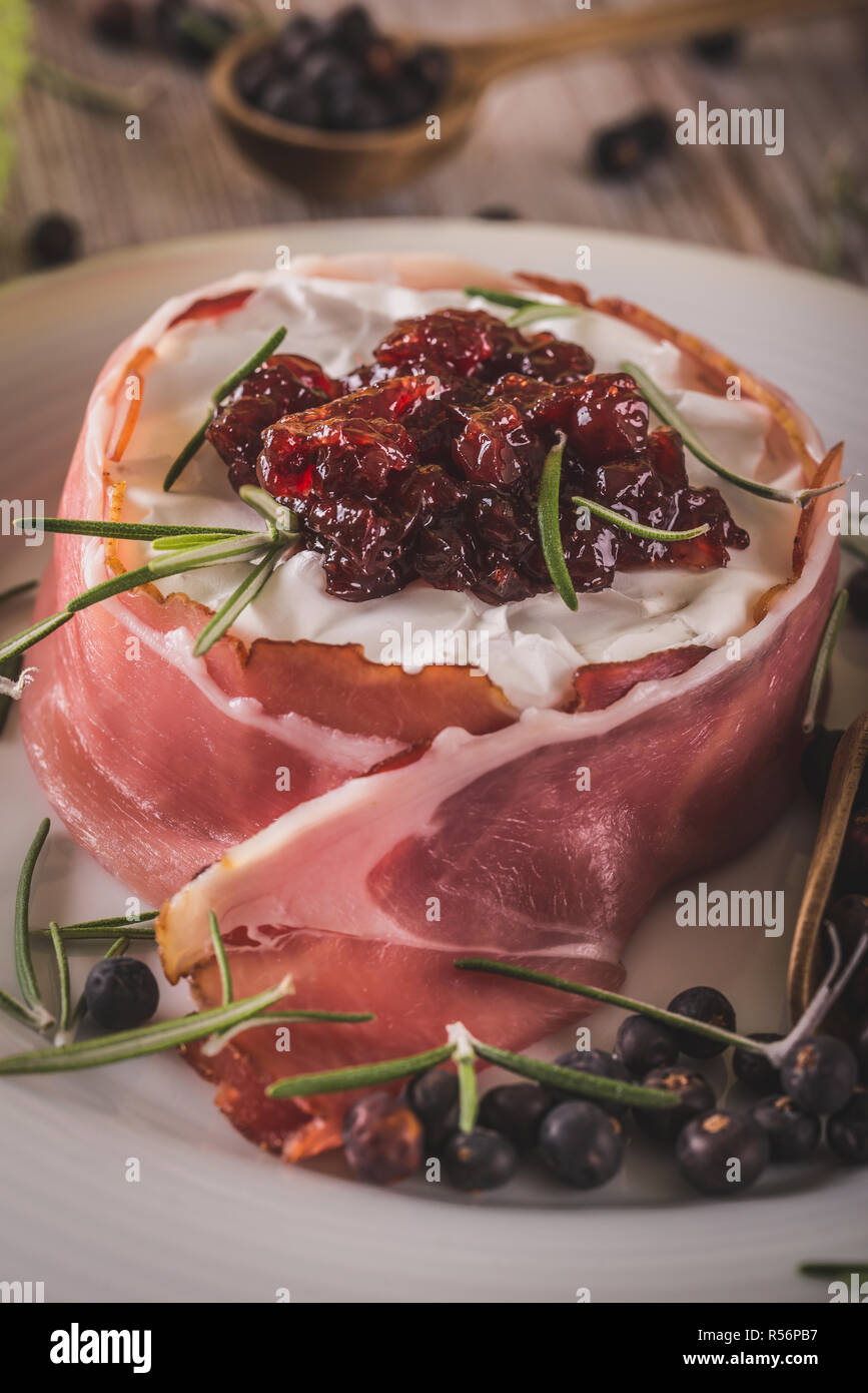 Vertical photo of whole camembert. Cheese is wrapped in dry ham and has ...