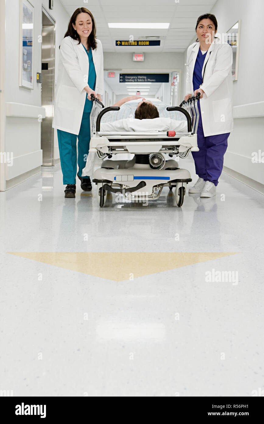 Doctors pushing patient in bed through corridor Stock Photo - Alamy