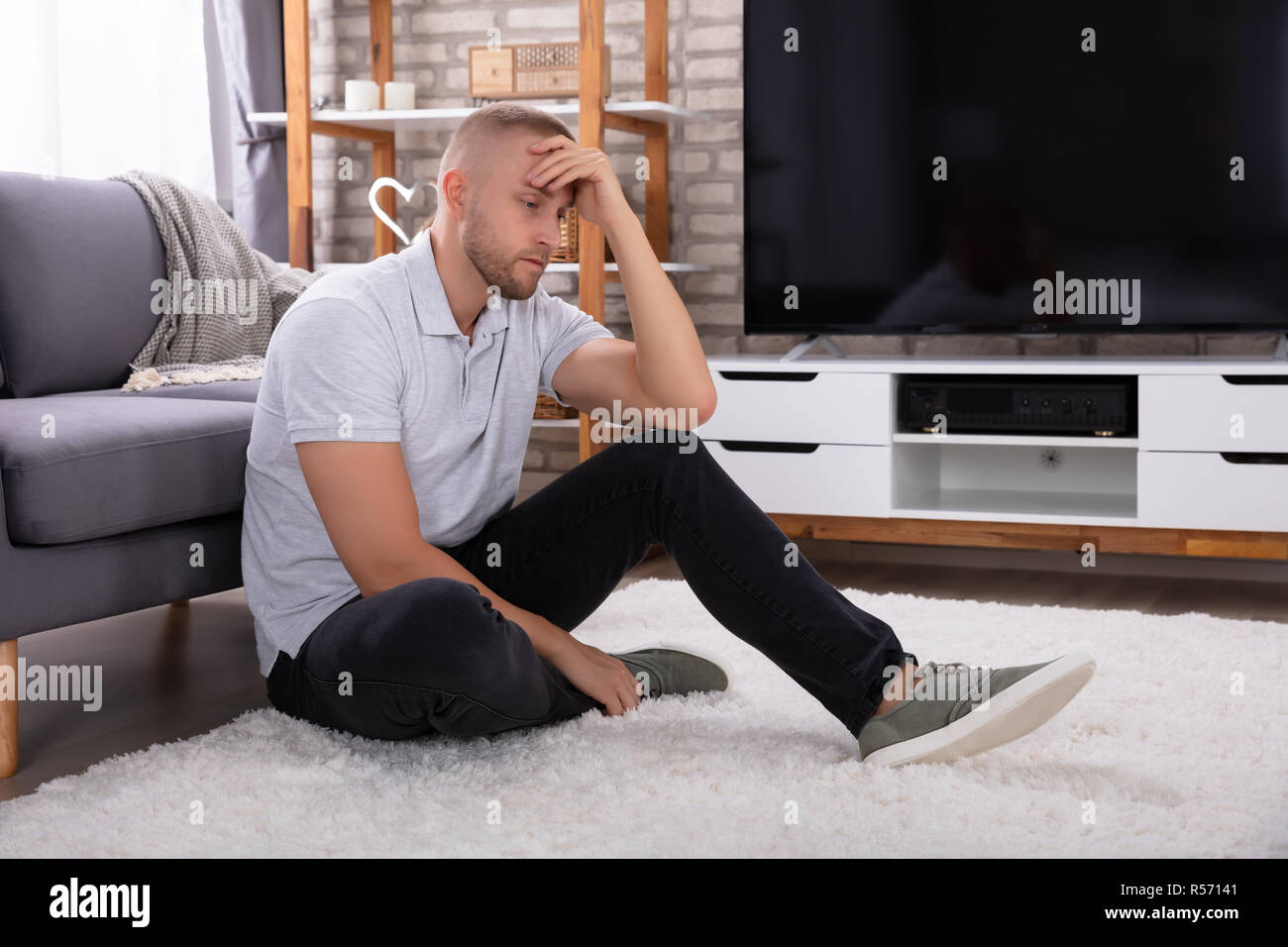 Side View Of A Upset Young Man Sitting Near Sofa Stock Photo - Alamy