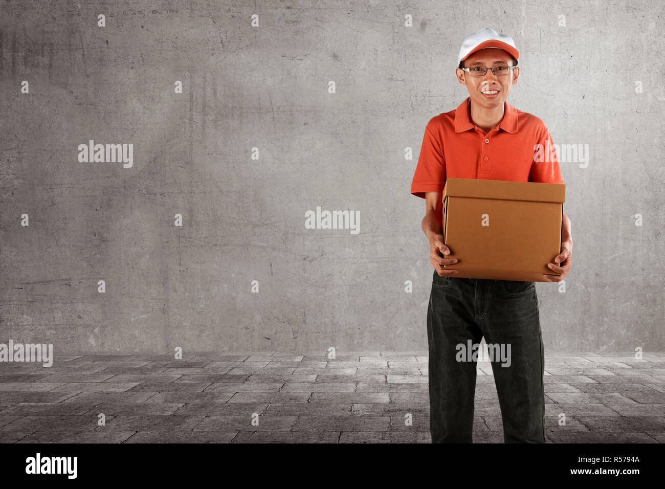 Cheerful asian courier standing with parcel Stock Photo - Alamy