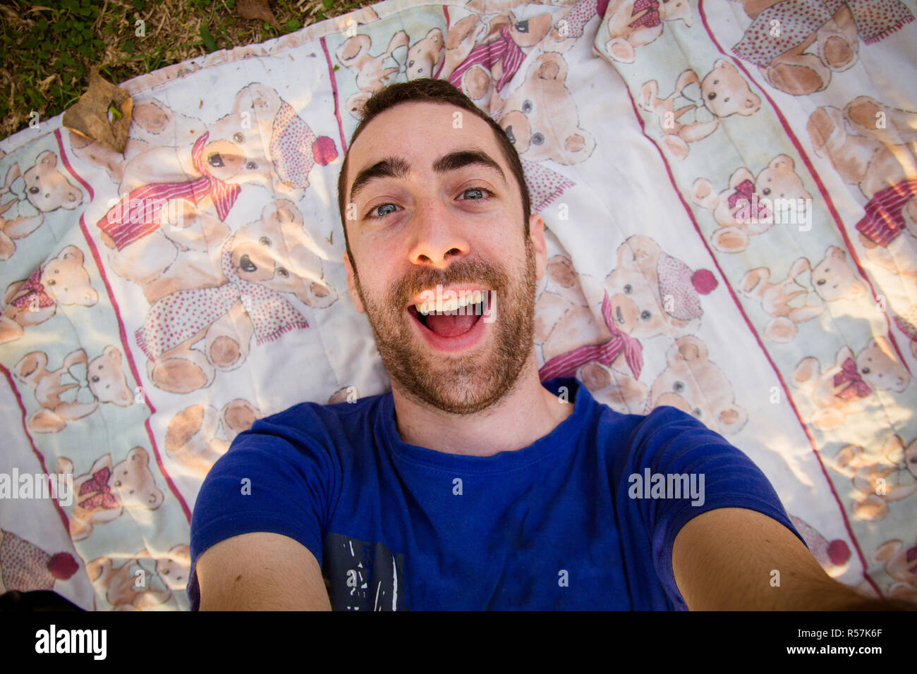 Young man lying on a sheet in the park and taking selfie picture with ...