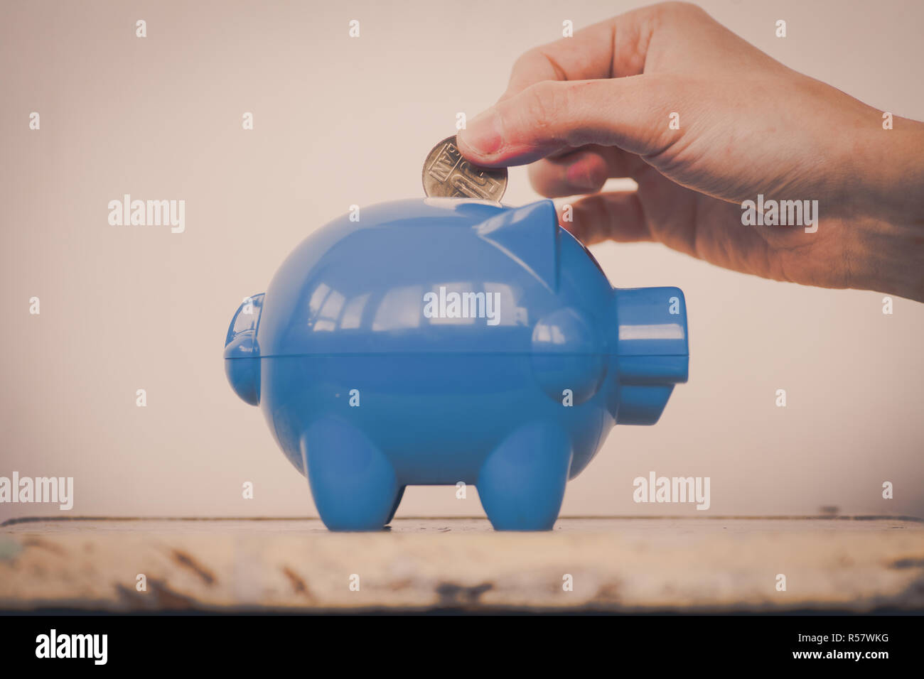 Adding coins to the piggy bank Stock Photo - Alamy