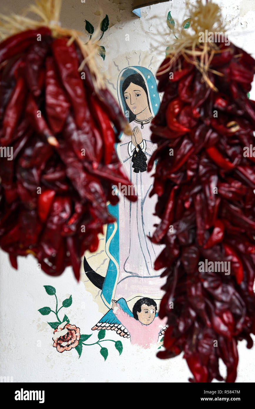 Red Chile ristras hang in front of a painting of Our Lady of Guadalupe ...