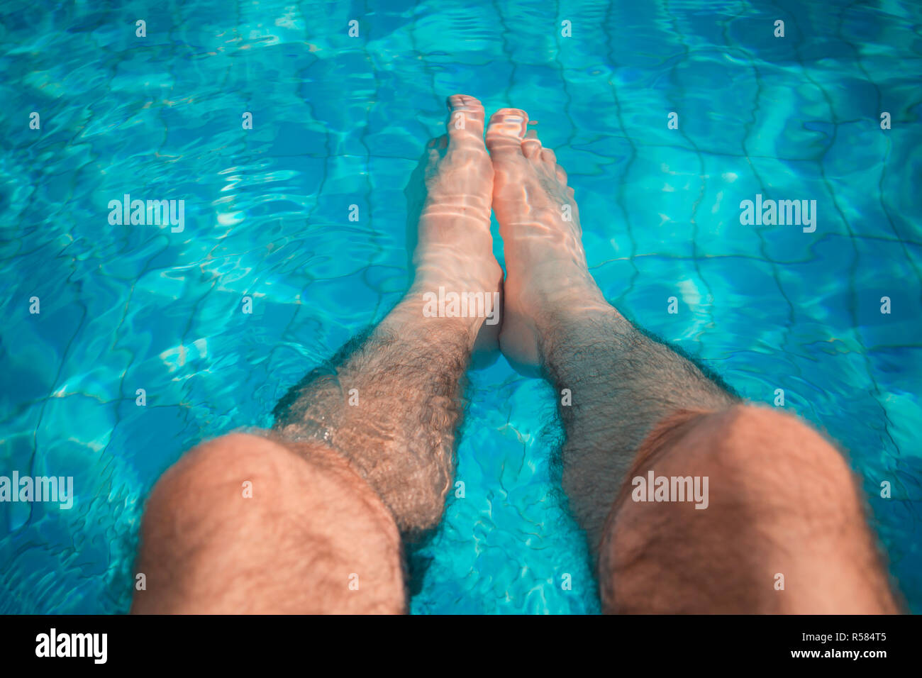 Young man relaxation at the swimming pool with his legs in the water ...