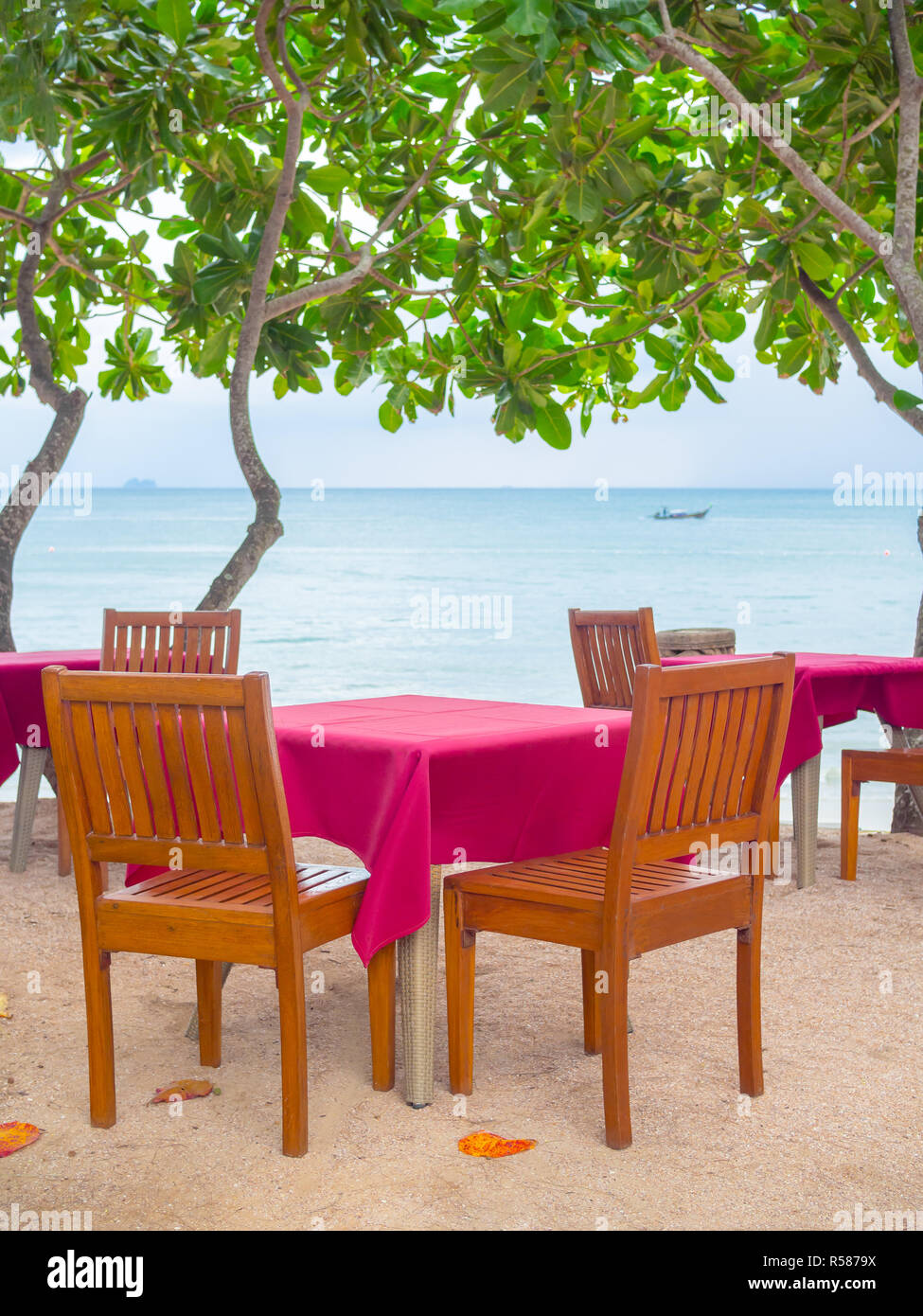 Wooden dinner table set with red tablecloth on the sand beach with the ...
