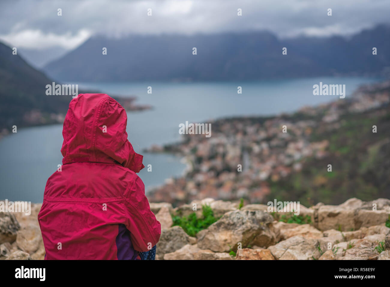 Girl in a waterproof red jacket sitting on the viewpoint and admiring ...