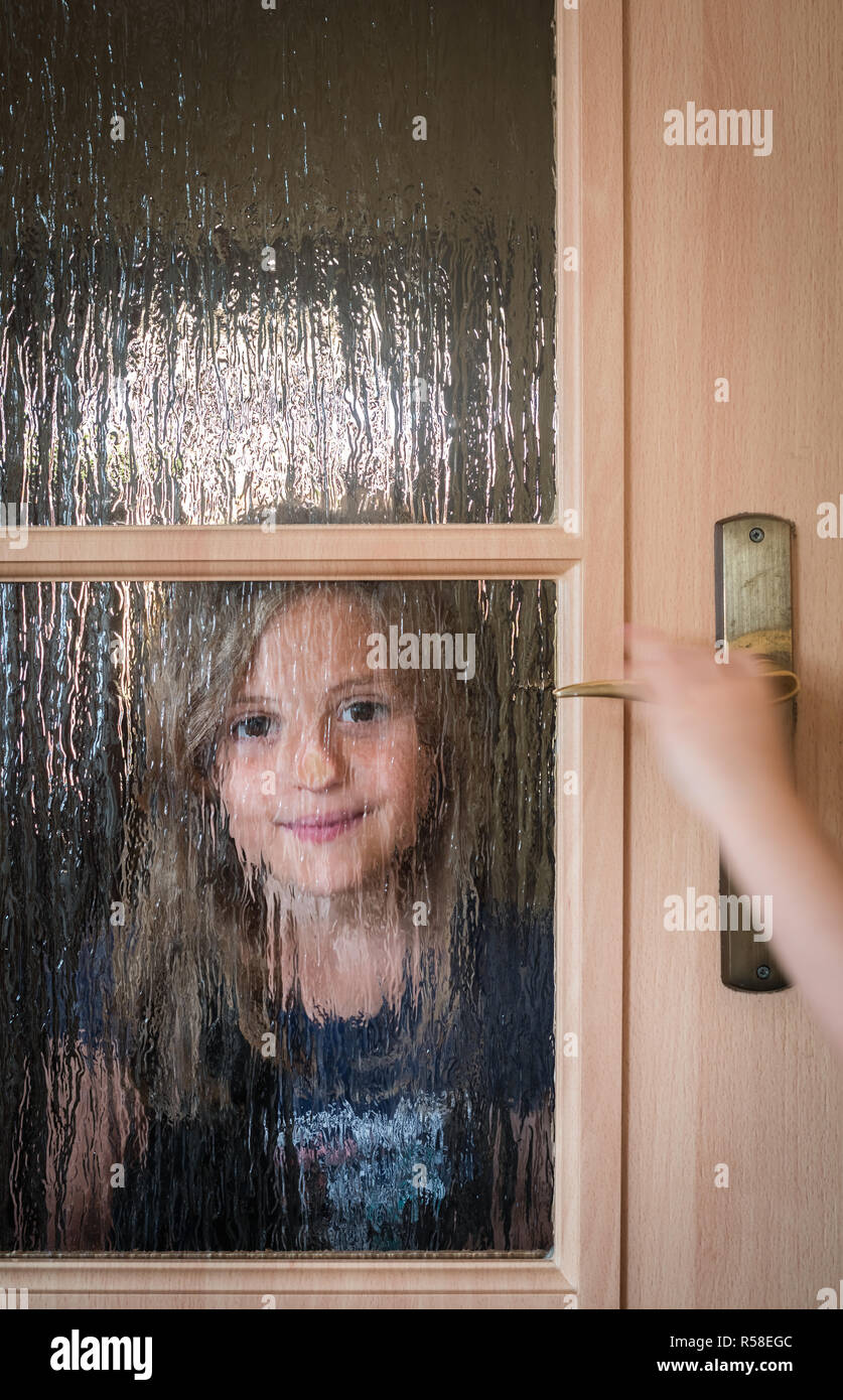 Portrait of a cute little Caucasian girl hiding behind a door with ...