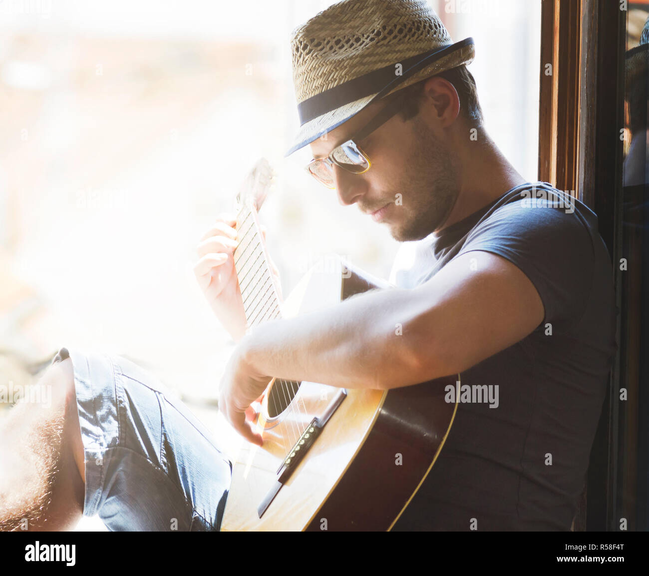 Portrait of young stylish guy with hat and sunglasses plays guitar at ...