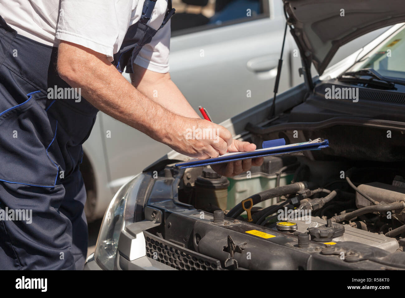 Auto mechanic checking car engine and writing on the clipboard Stock ...