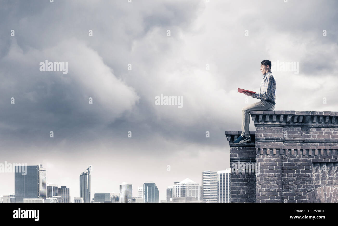 Man on roof edge reading book and cityscape at background Stock Photo ...