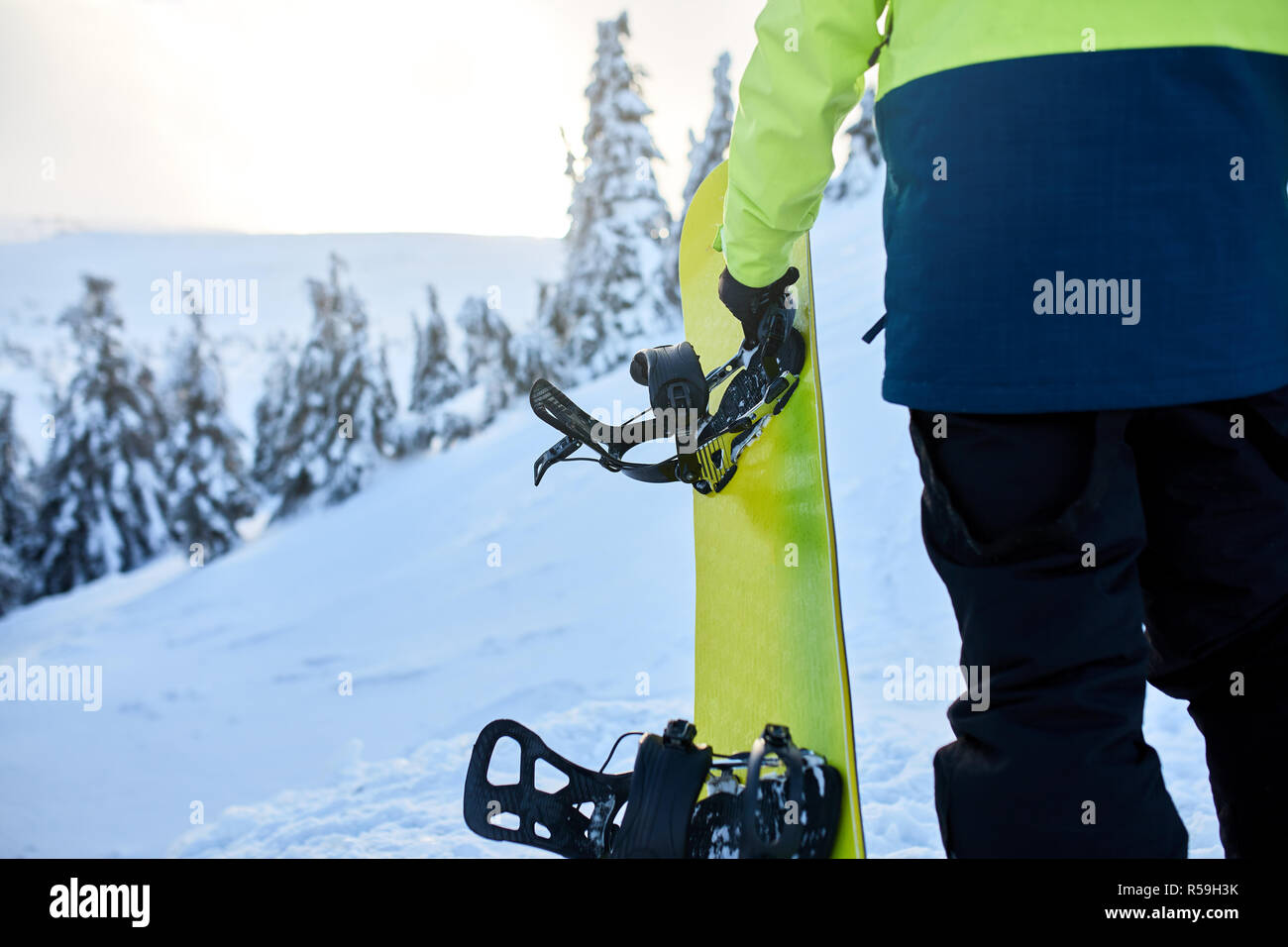 Back view of snowboarder climbing with his board on the mount for ...