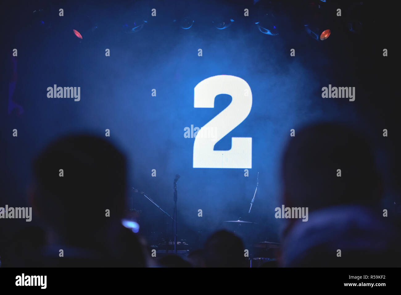 Silhouettes of a concert crowd waiting to start. On the screen, a ...