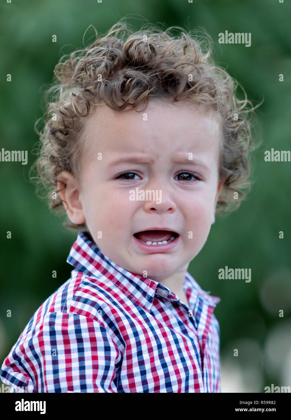 Sad baby with curly hair crying in the garden Stock Photo - Alamy