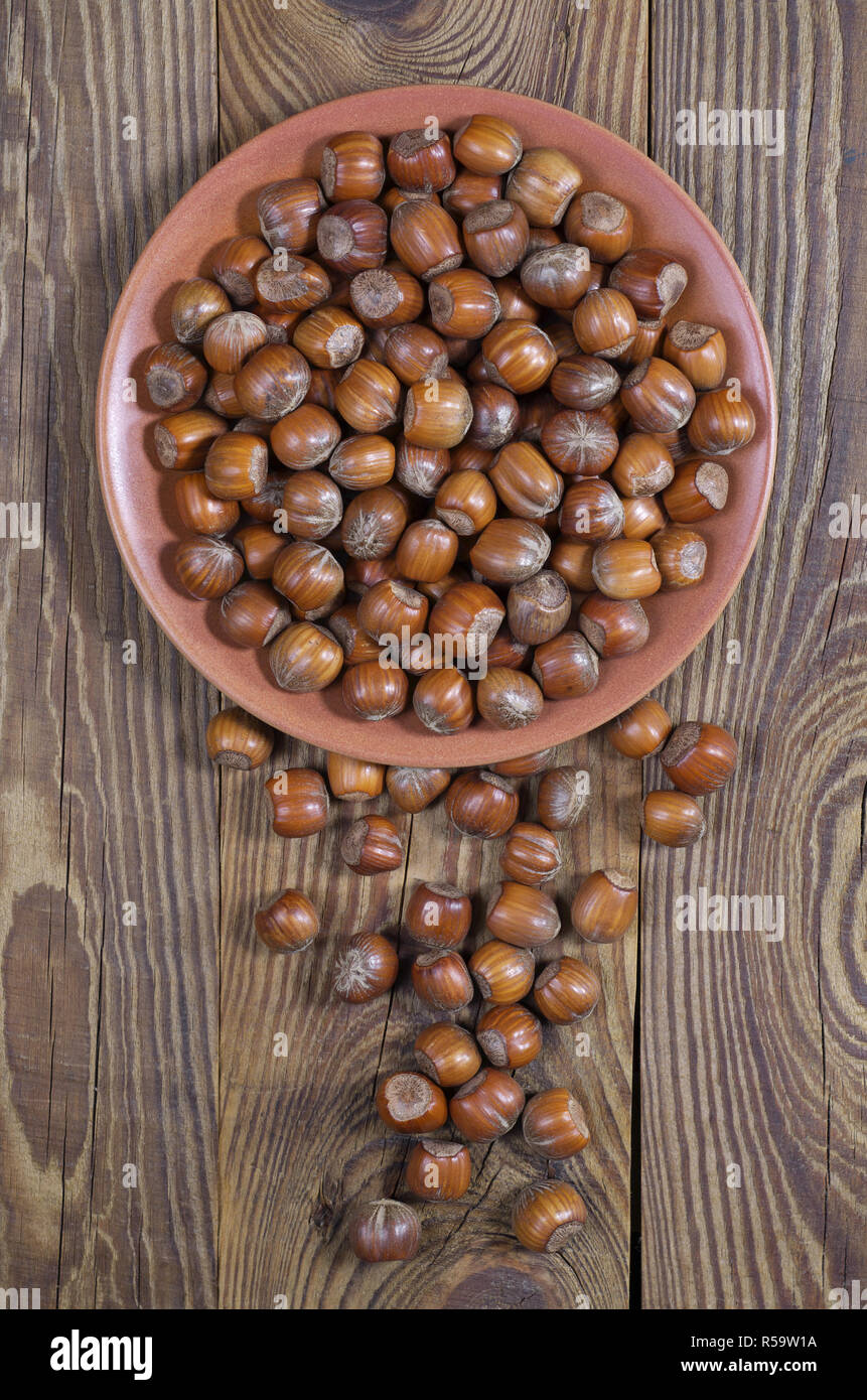 Hazelnuts in a brown plate and near are located on an old wooden table ...