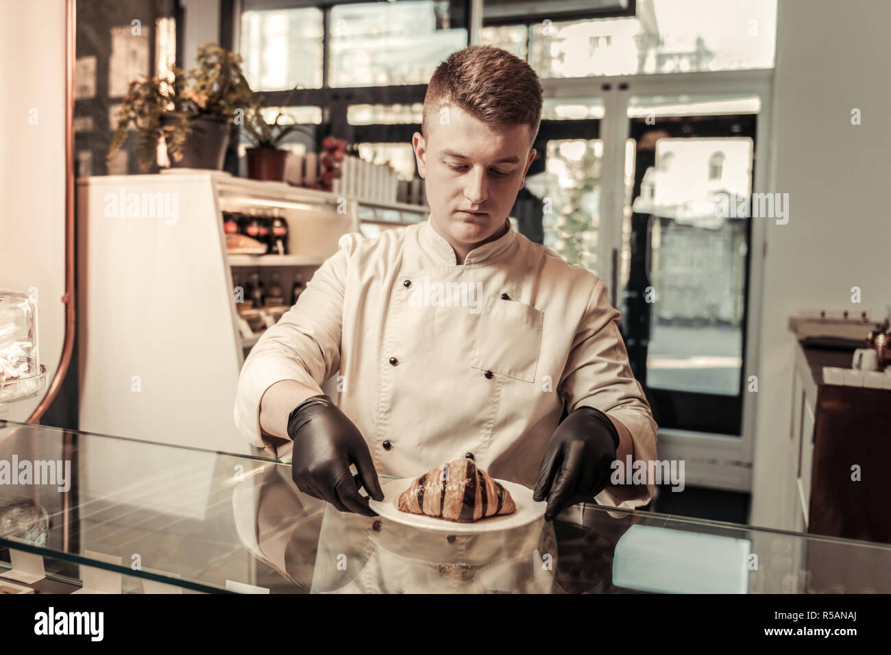 Best bakery. Nice professional baker holding a plate with a croissant ...