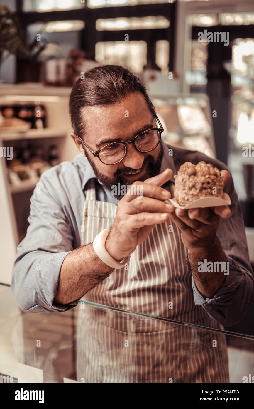 Professional baker. Delighted happy man looking at the cake while ...