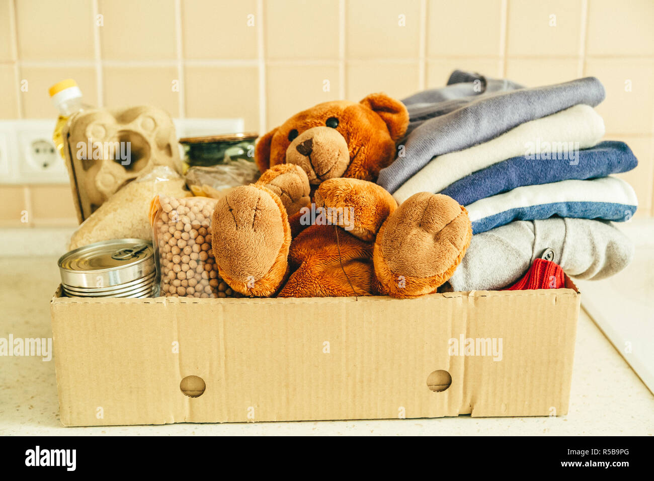 Donating concept - food, clothes, toys in cardboard, kitchen background ...