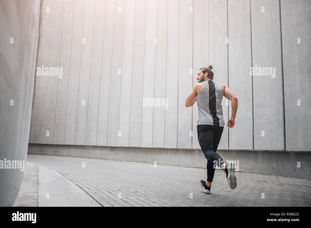 Strong and well-built runner jogging through concrete corridor. He ...