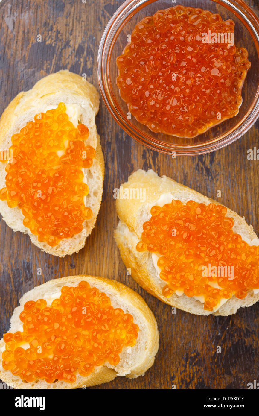Sandwiches with red caviar and butter in plate on wooden table. Top ...