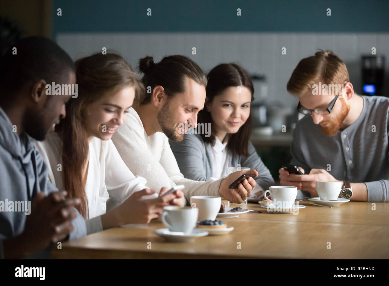 Diverse young people sit in cafe having fun using gadgets, multiethnic students spend time ...