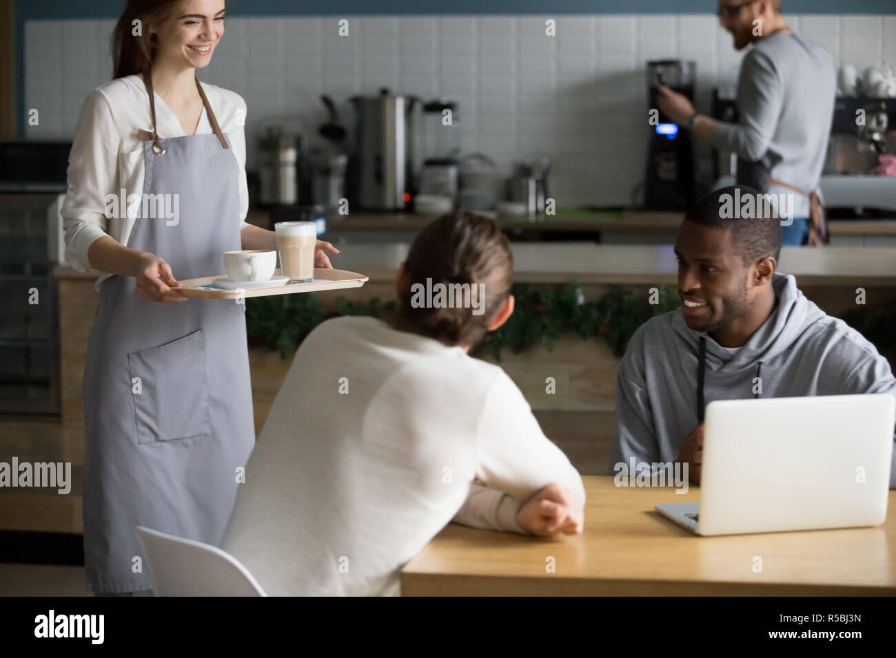Smiling pretty girl serve coffee to millennial male cafe visitors ...