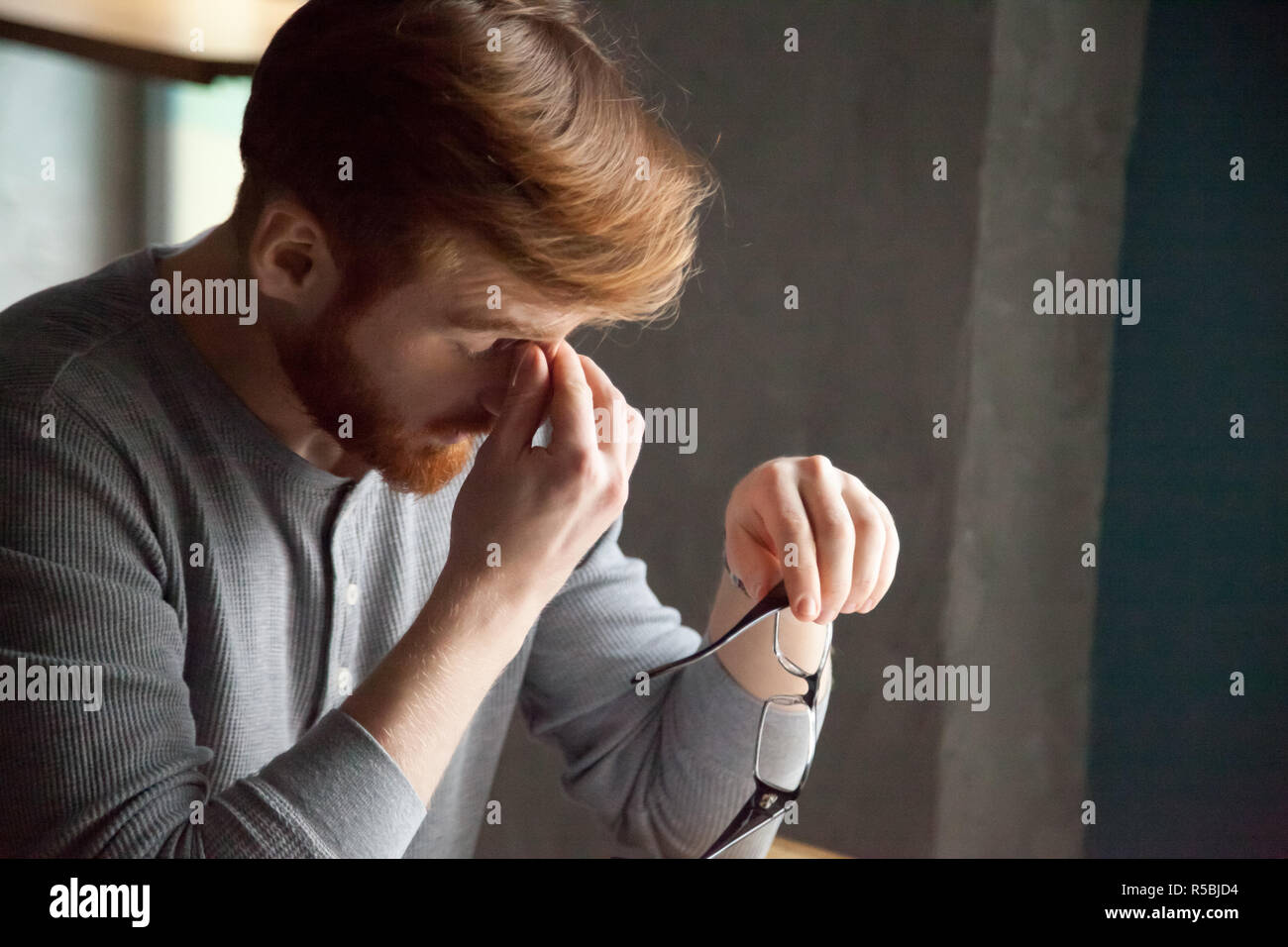 Tired red haired man take glasses off working too long at computer ...