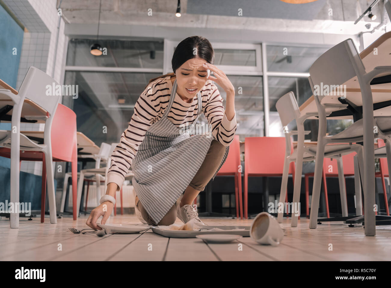 Young inexperienced waitress feeling nervous after dropping the tray ...